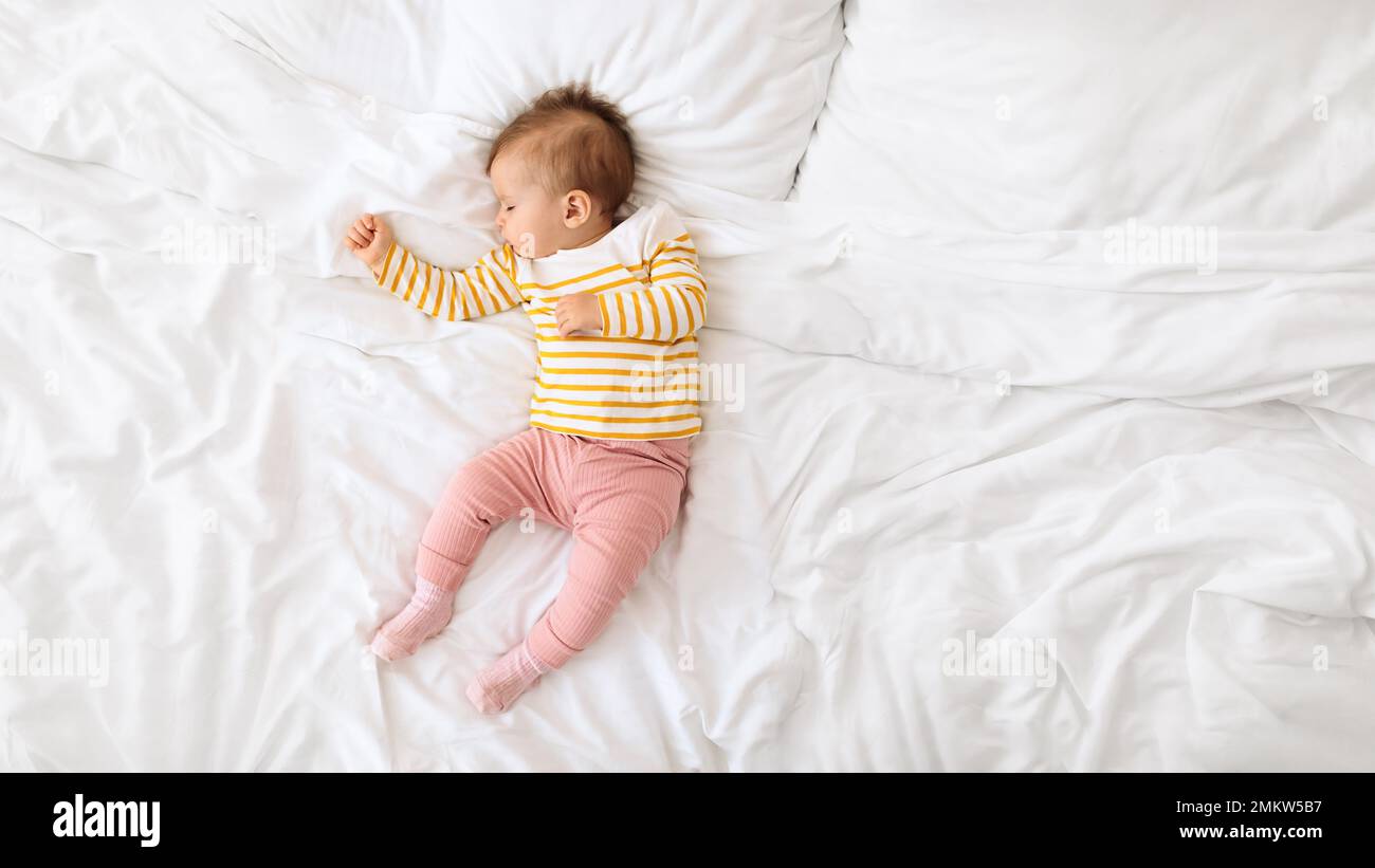 High-angle view of adorable baby girl napping on white blanket on bed ...
