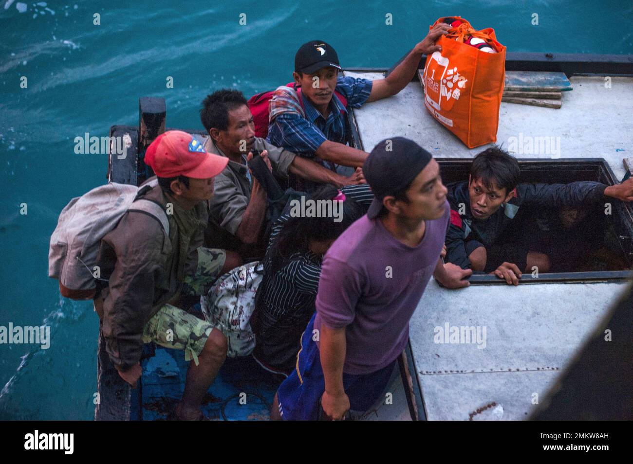 Residents of Sebuku Island wait with their belongings before boarding ...