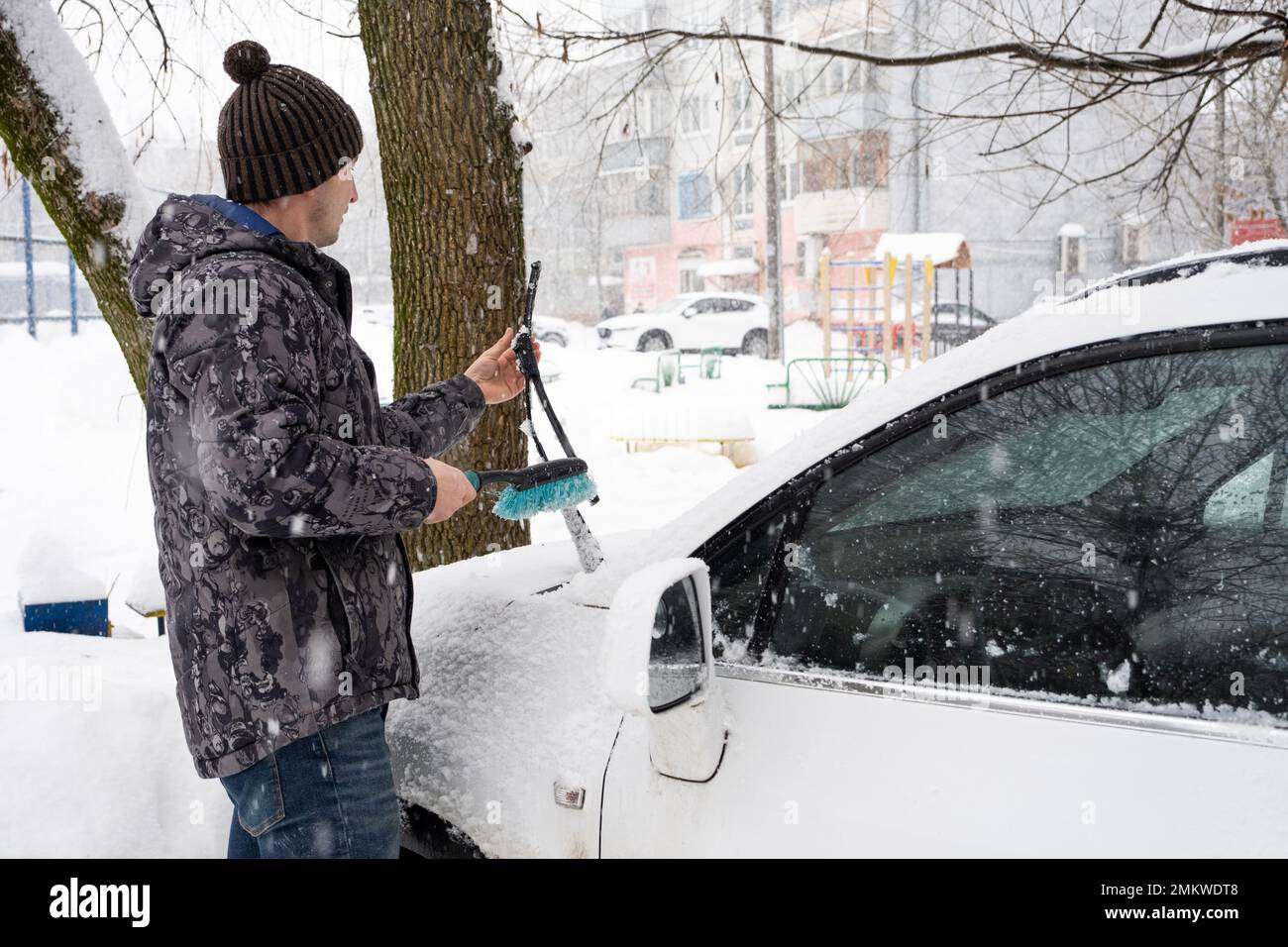 A man brushes snow from a car after a snowfall. Road safety, difficult ...