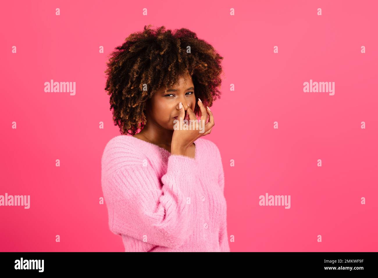 Sad dissatisfied upset young black curly lady in casual covering nose ...