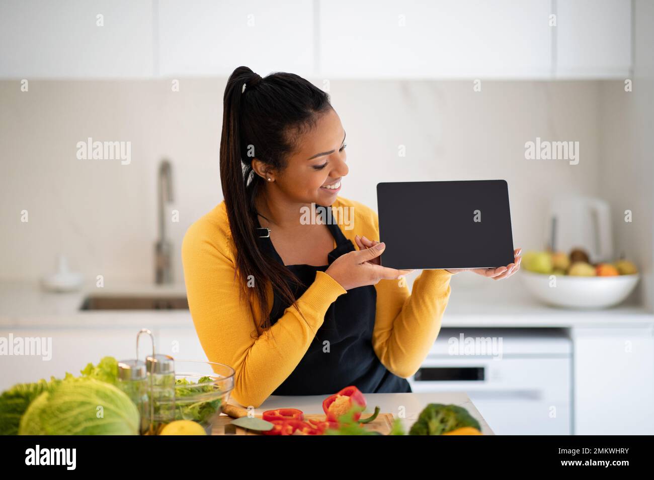 Cheerful millennial african american female in apron show tablet with ...