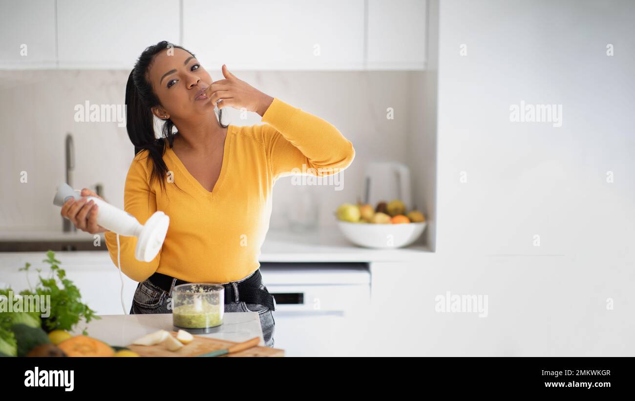 Cheerful millennial african american lady make smoothie with blender ...
