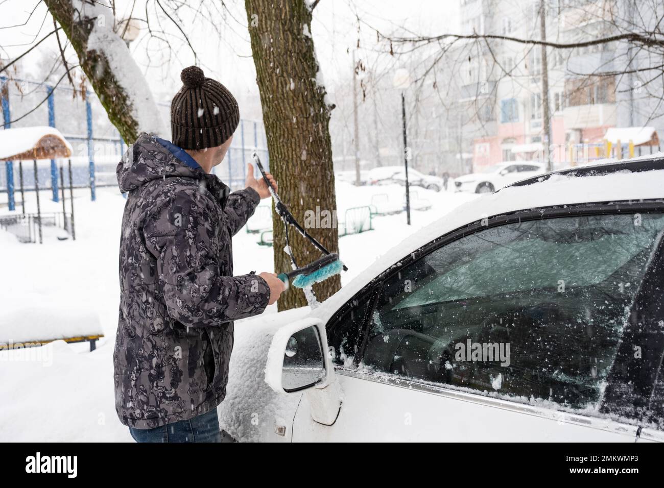 A man brushes snow from a car after a snowfall. Road safety, difficult ...