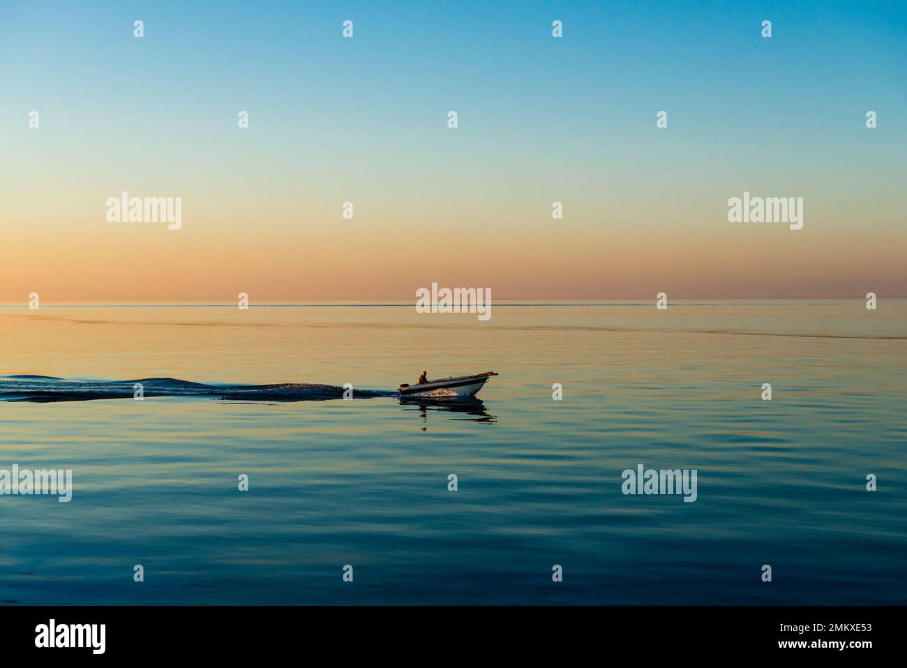 A fisherman drives his motor boat through the calm sea on the coast of ...