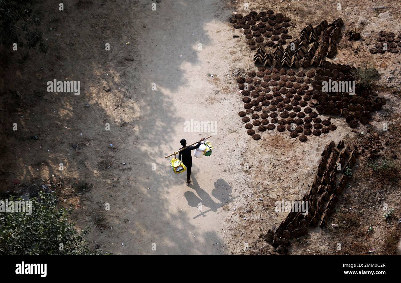 An Indian man carries plastic buckets as he walks past cow dung cakes ...