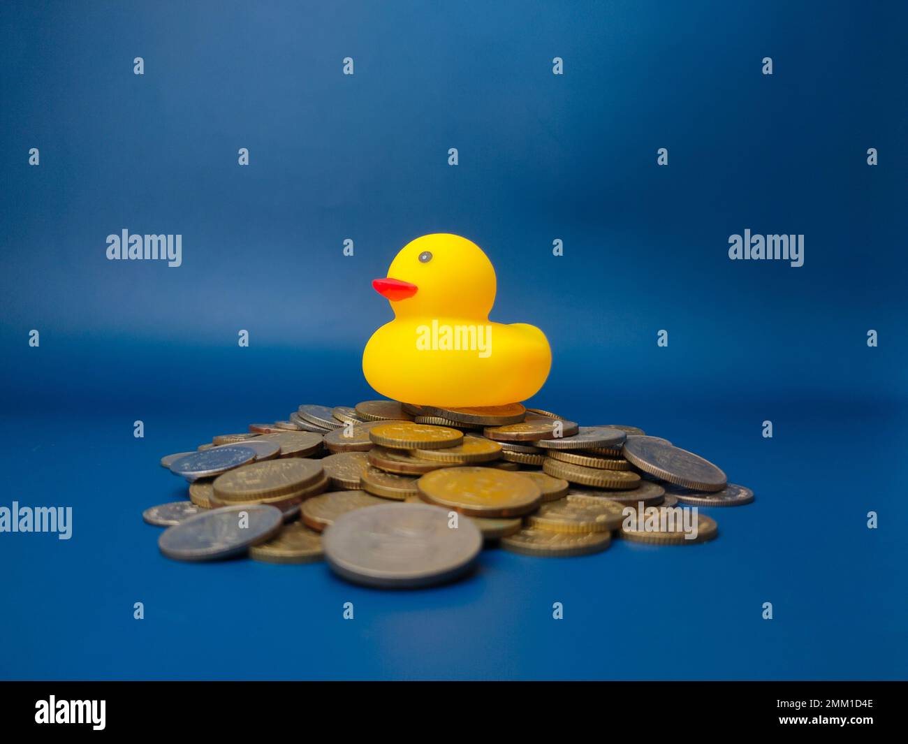 A toy yellow duck is on top of a stack of coins on a blue background ...