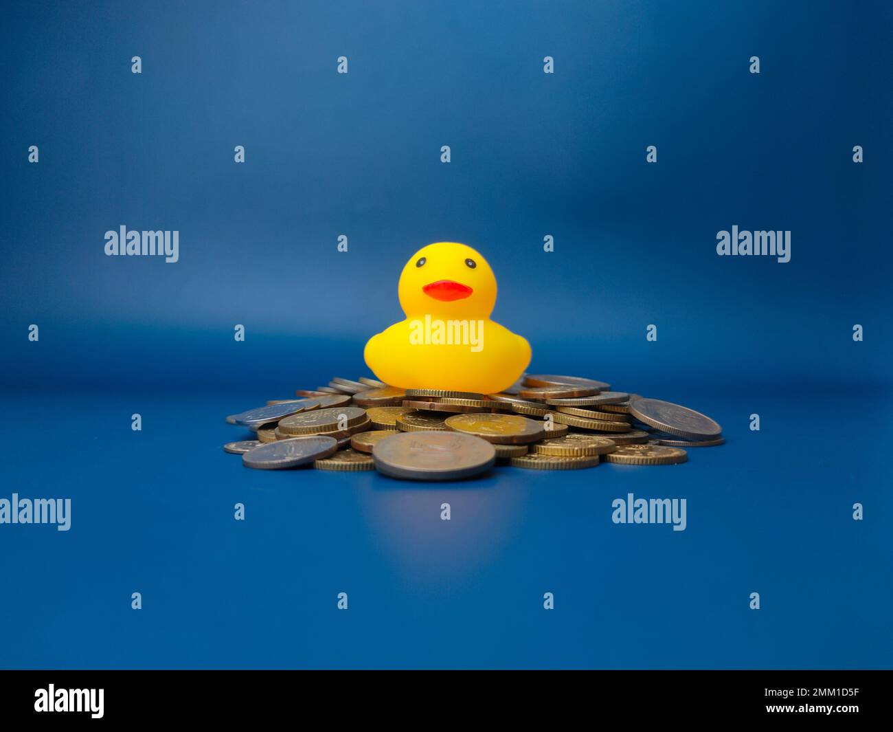 A toy yellow duck is on top of a stack of coins on a blue background ...