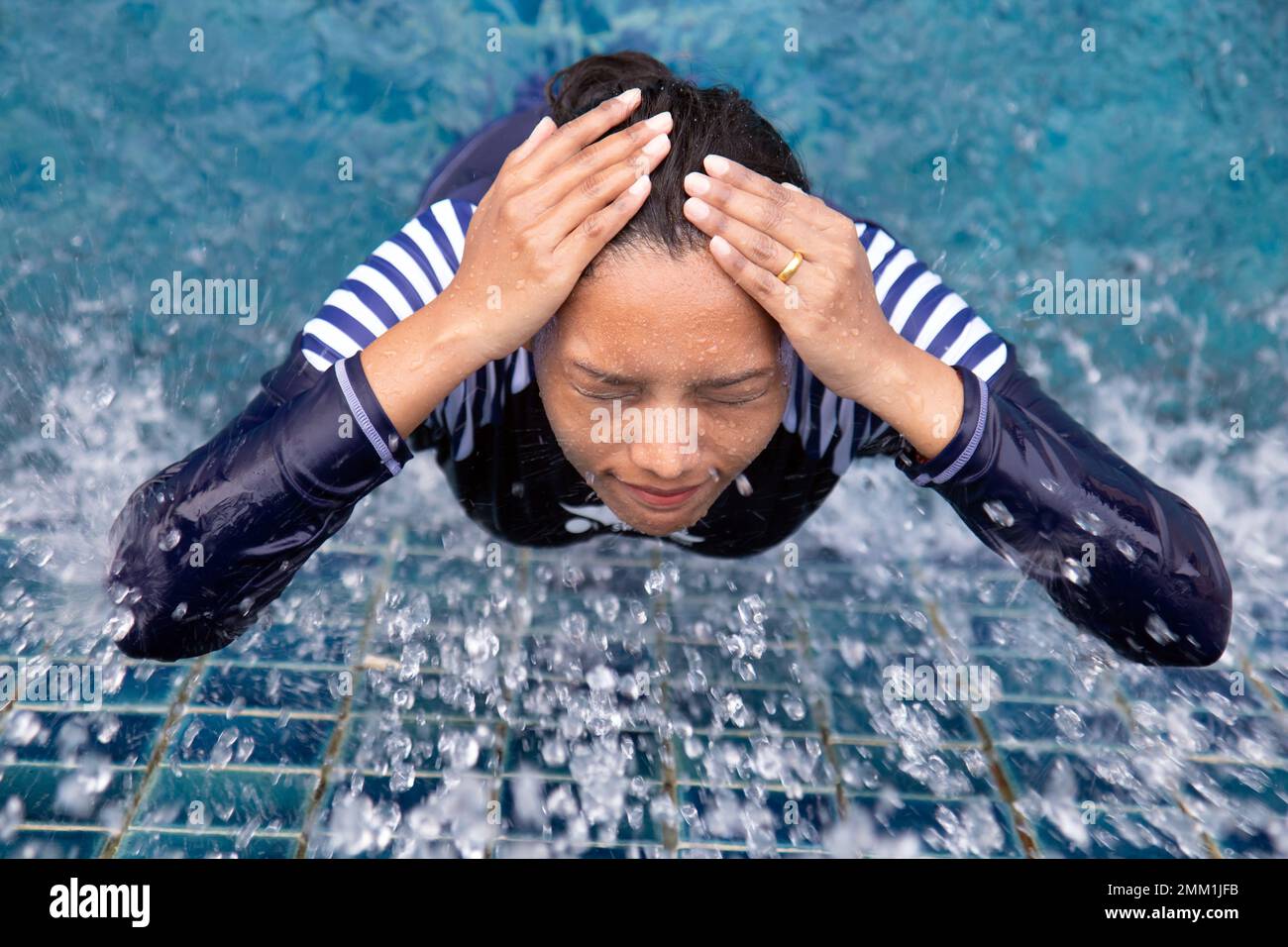 Young Woman In Full Body Swimsuit Standing Under Waterfall In Swimming