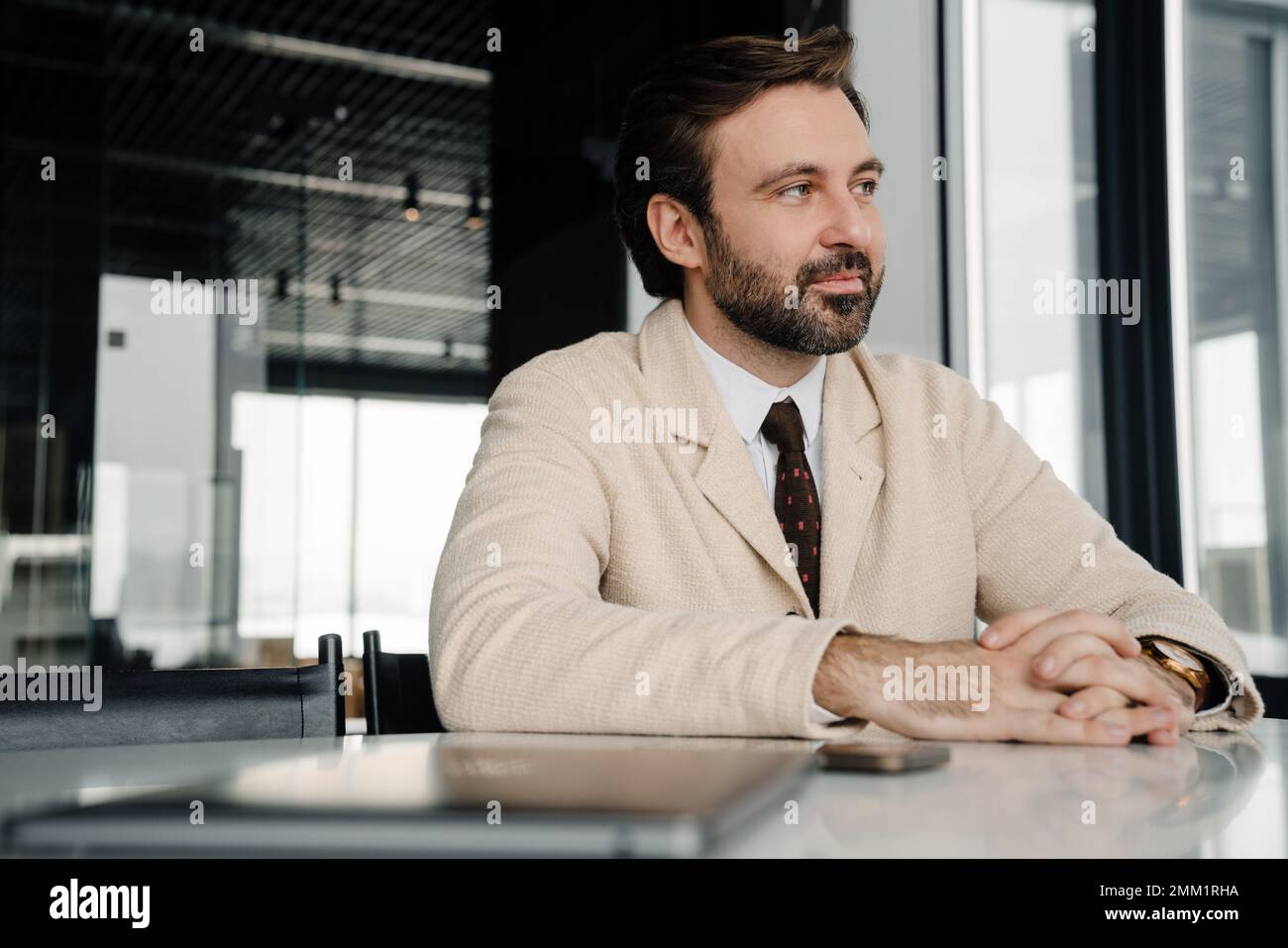 Adult businessman in beige suit sitting by table with intertwined ...