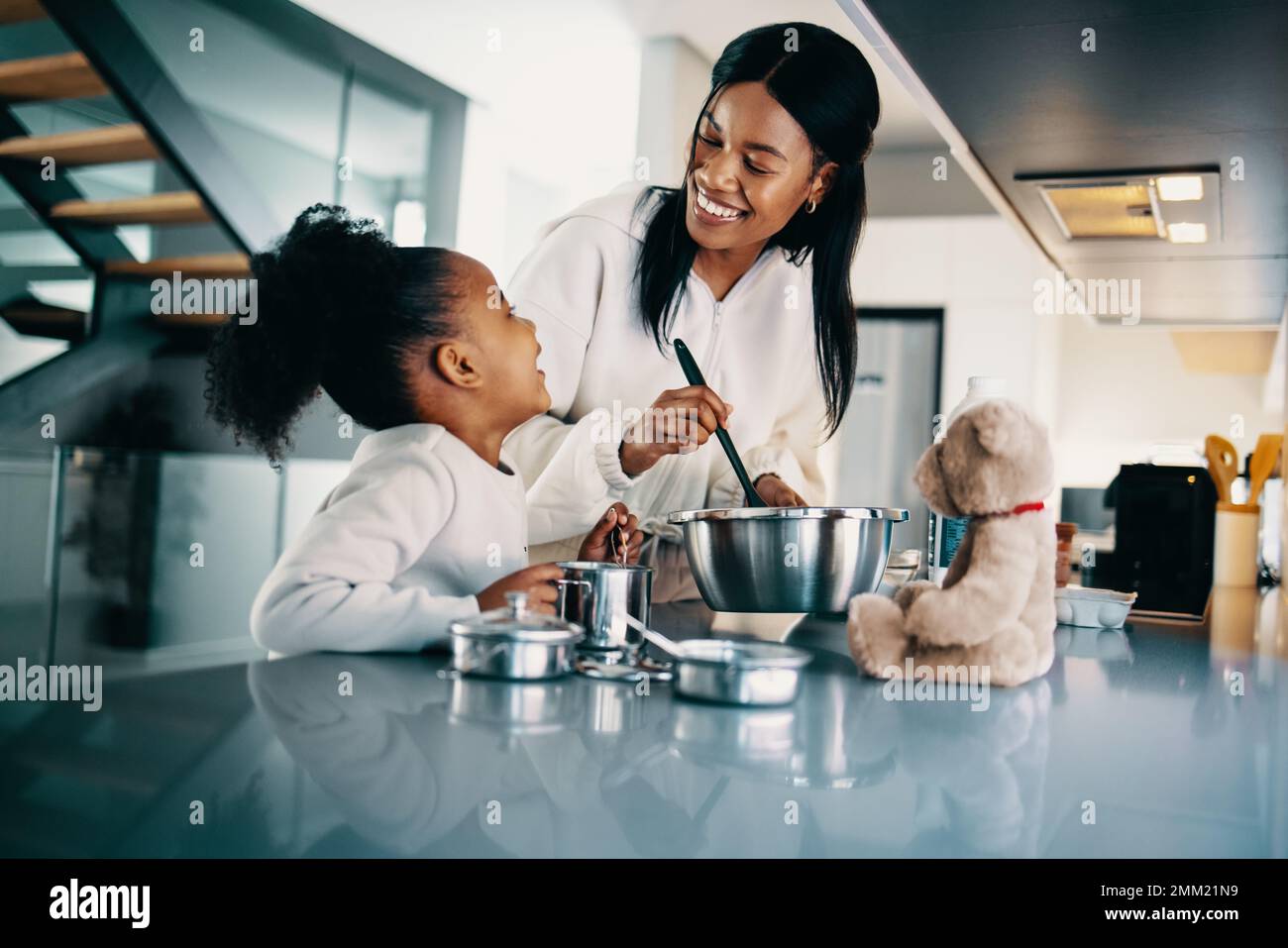 Little girl smiling at her mother as she is helping her make cake in ...