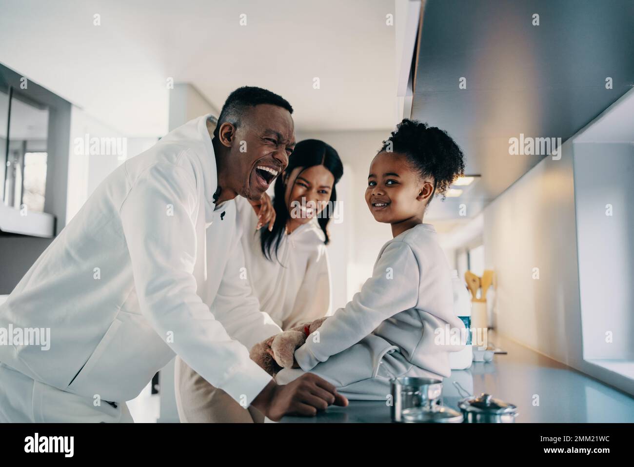 Parents laughing happily in the kitchen with their young daughter. Mom ...