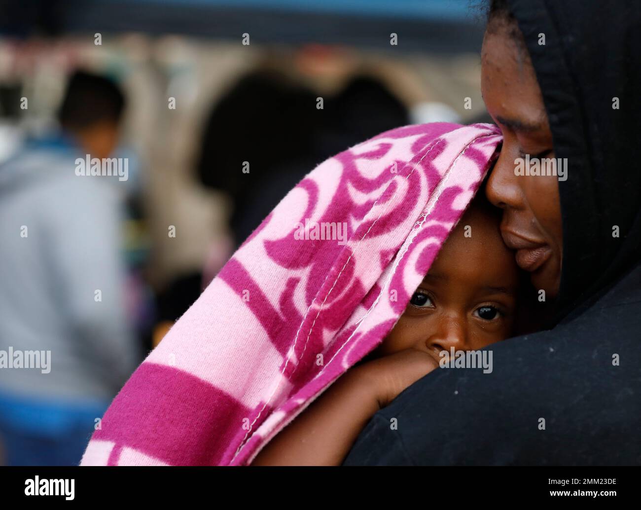 A Haitian migrant woman holds her baby as she waits in line to put her ...