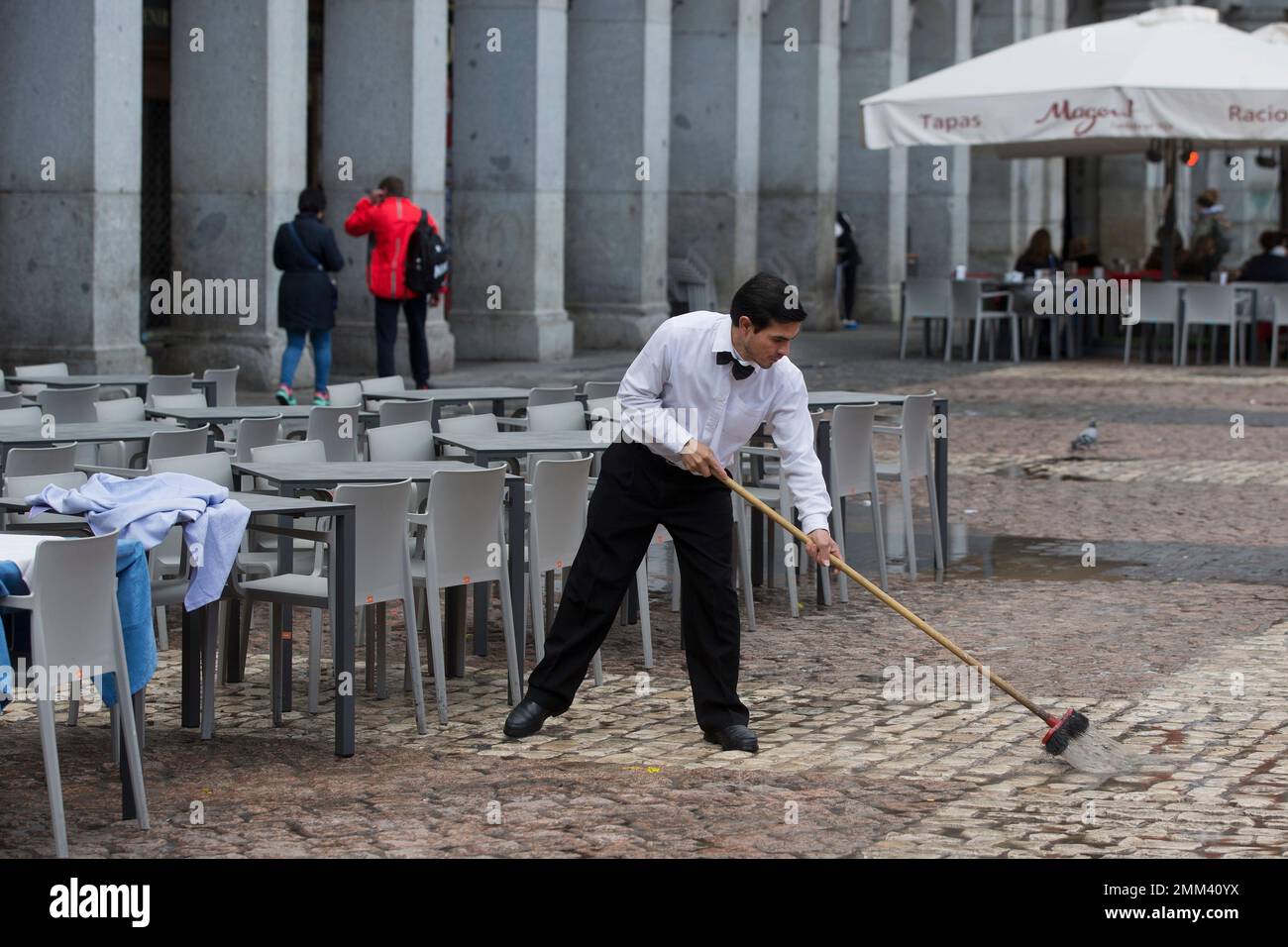 A waiter sweeps rain water from an empty terrace bar in Plaza Mayor in ...