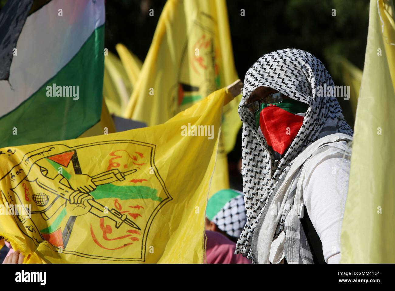 A Palestinian covers her face with a national flag while waving yellow ...