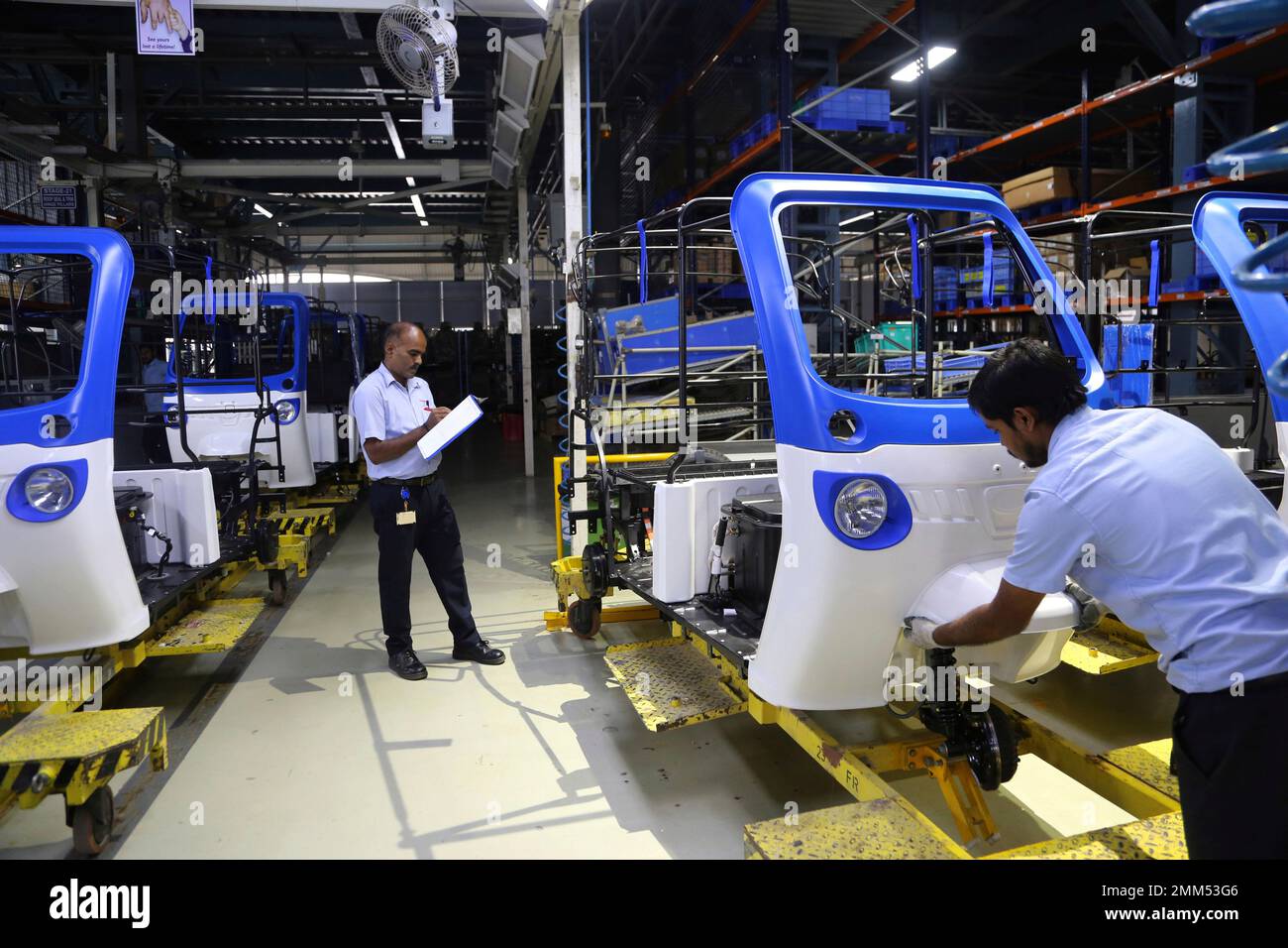 Indian workers perform a check on three-wheeler electric vehicles at an ...