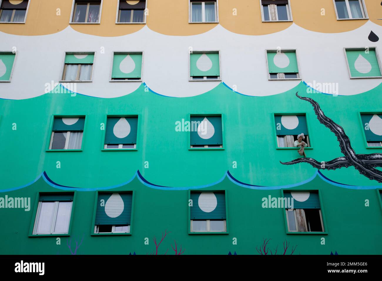 A woman peers out from a window of a building decorated by a murals by ...