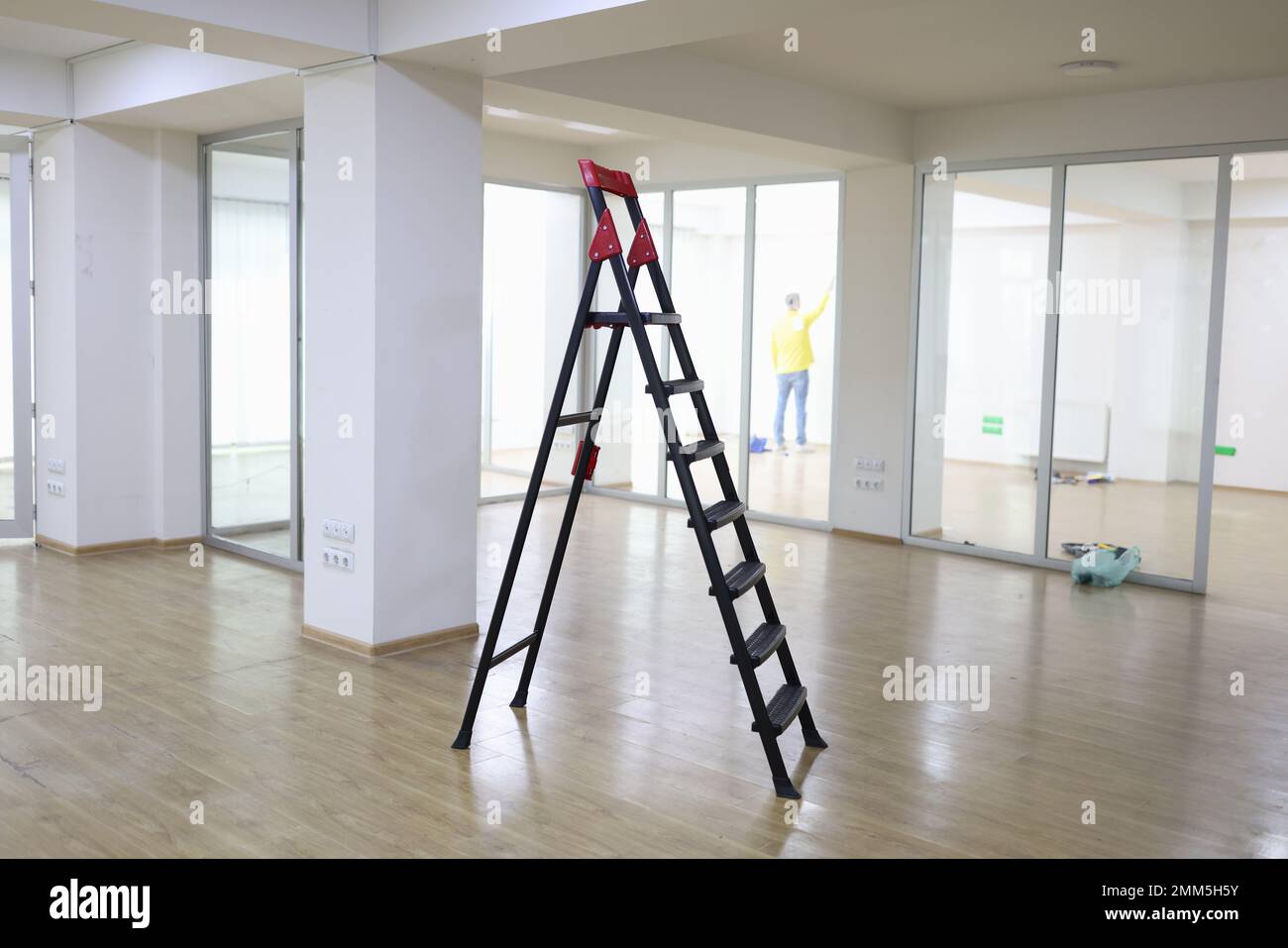 Metal ladder standing in center of empty office, worker repairing wall ...