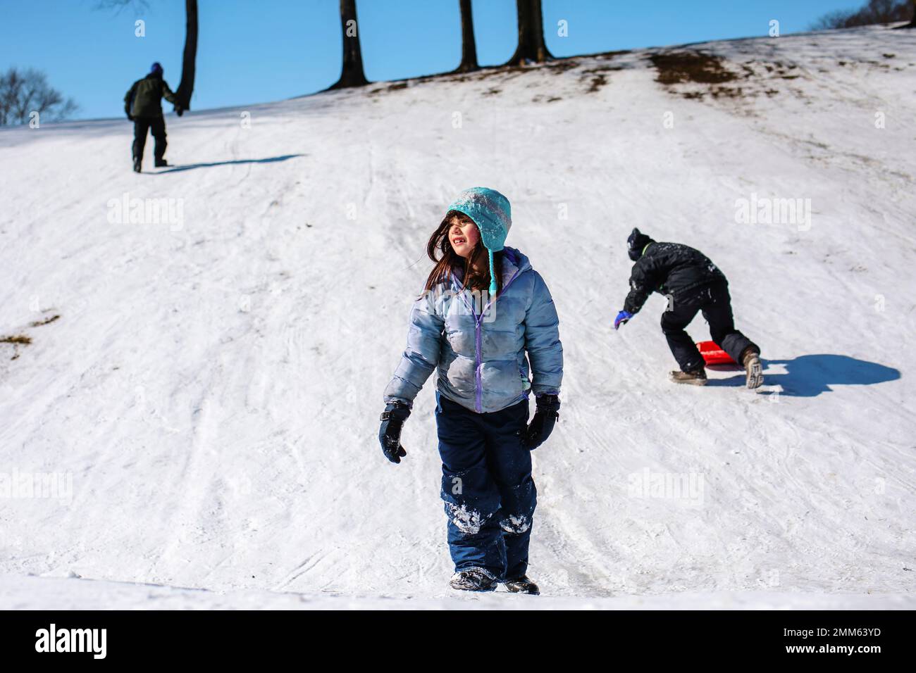 A little girl sleds on a hill with family in winter Stock Photo - Alamy