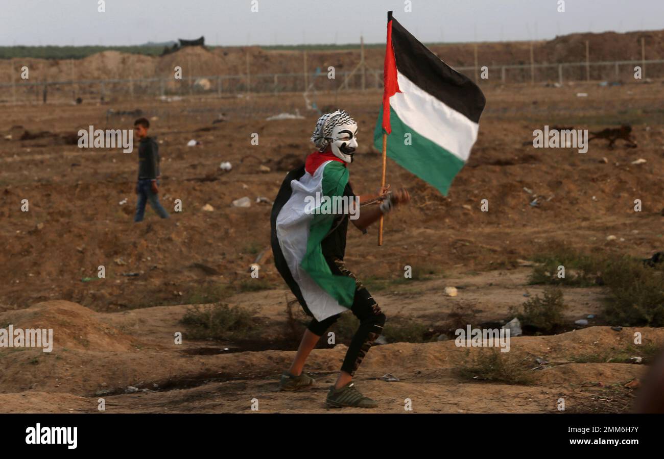 A masked protester waves his national flag near the fence of Gaza Strip ...