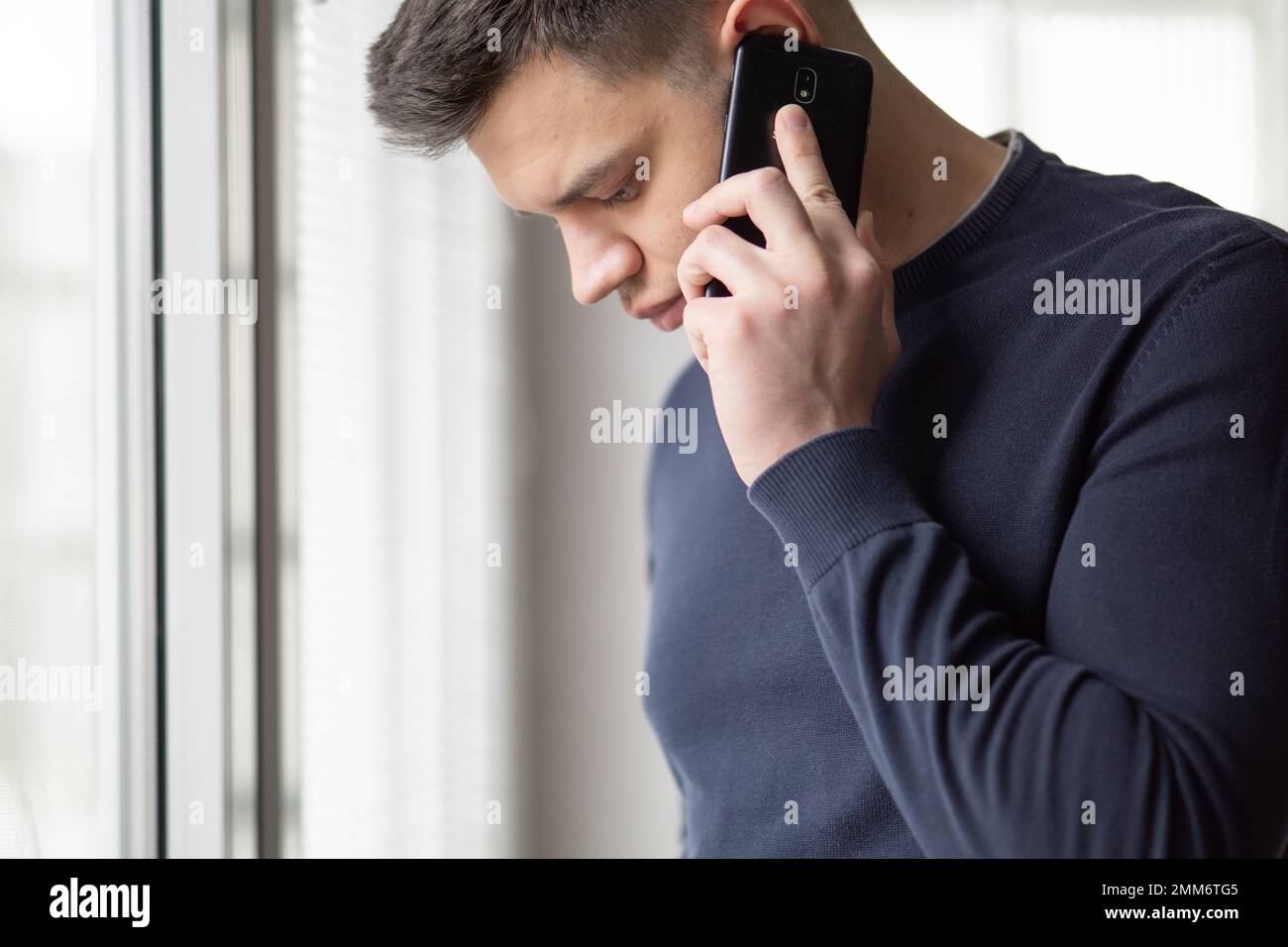 Man standing next to windows at home and speaking on his phone. Close ...
