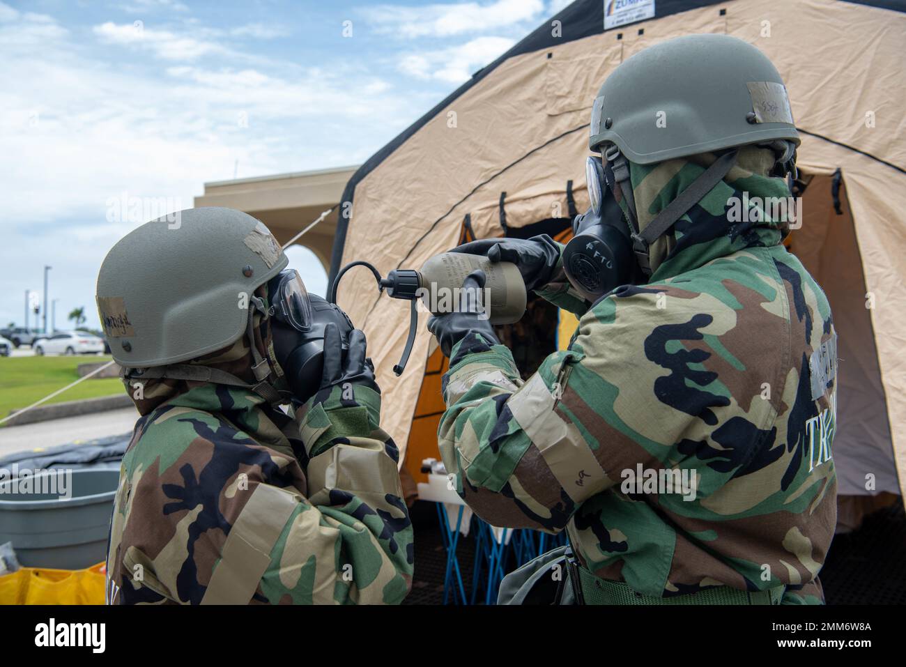 U.S. Air Force Airmen with the 36th Medical Group help each other drink through their gas masks ...
