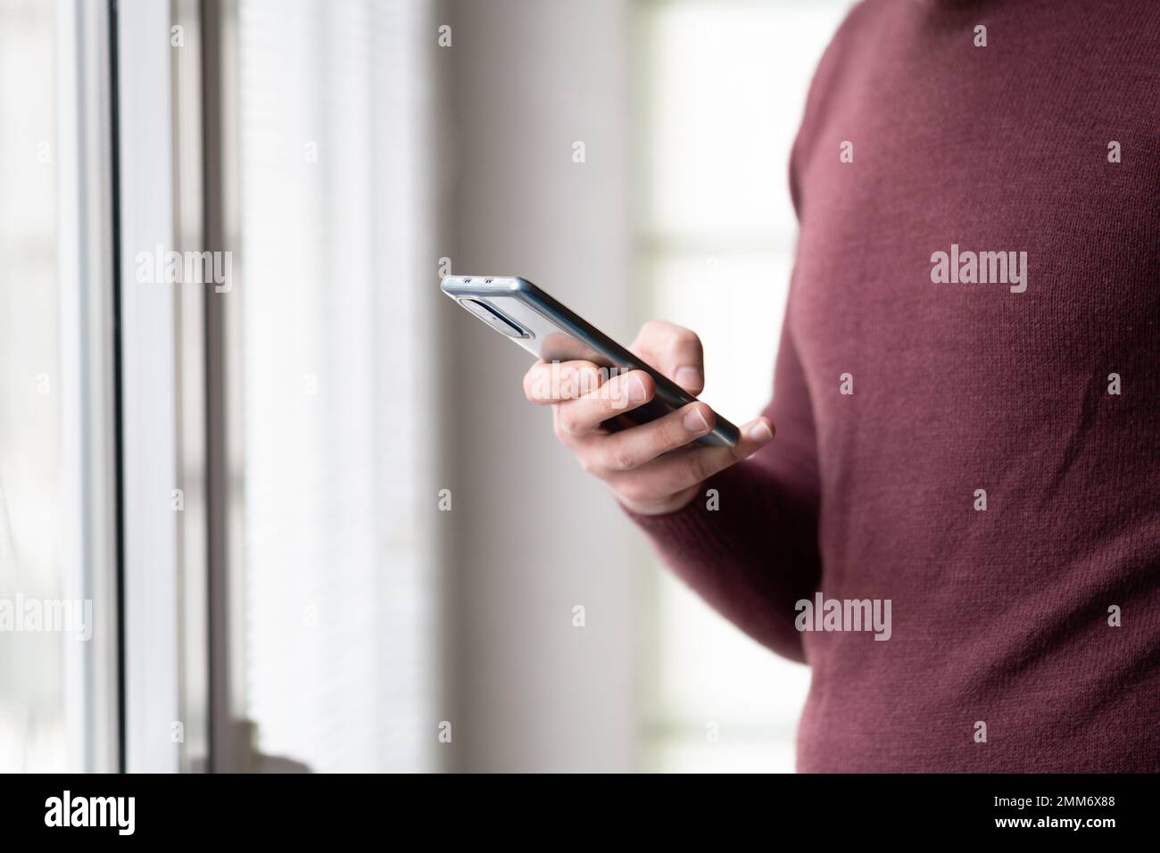 Man standing next to windows at home and using smartphone. Close up of ...