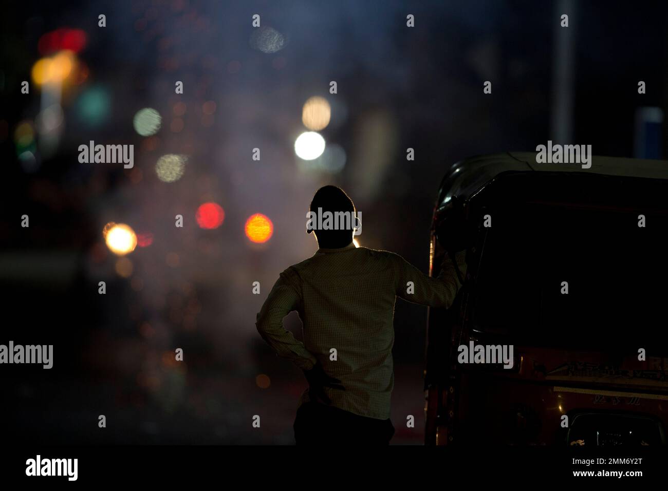 An Indian auto rickshaw driver waits at a street and watches others ...