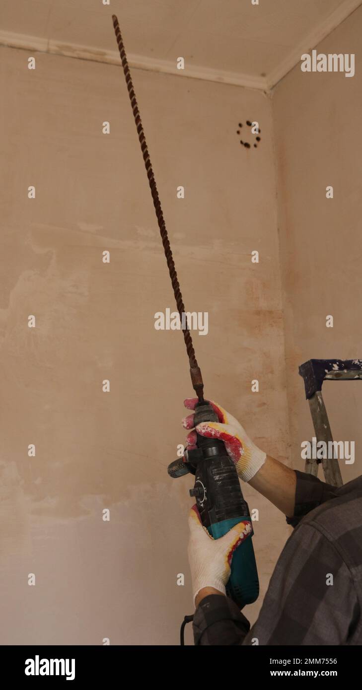 a worker in gloves with a puncher with a long drill in his hands ...