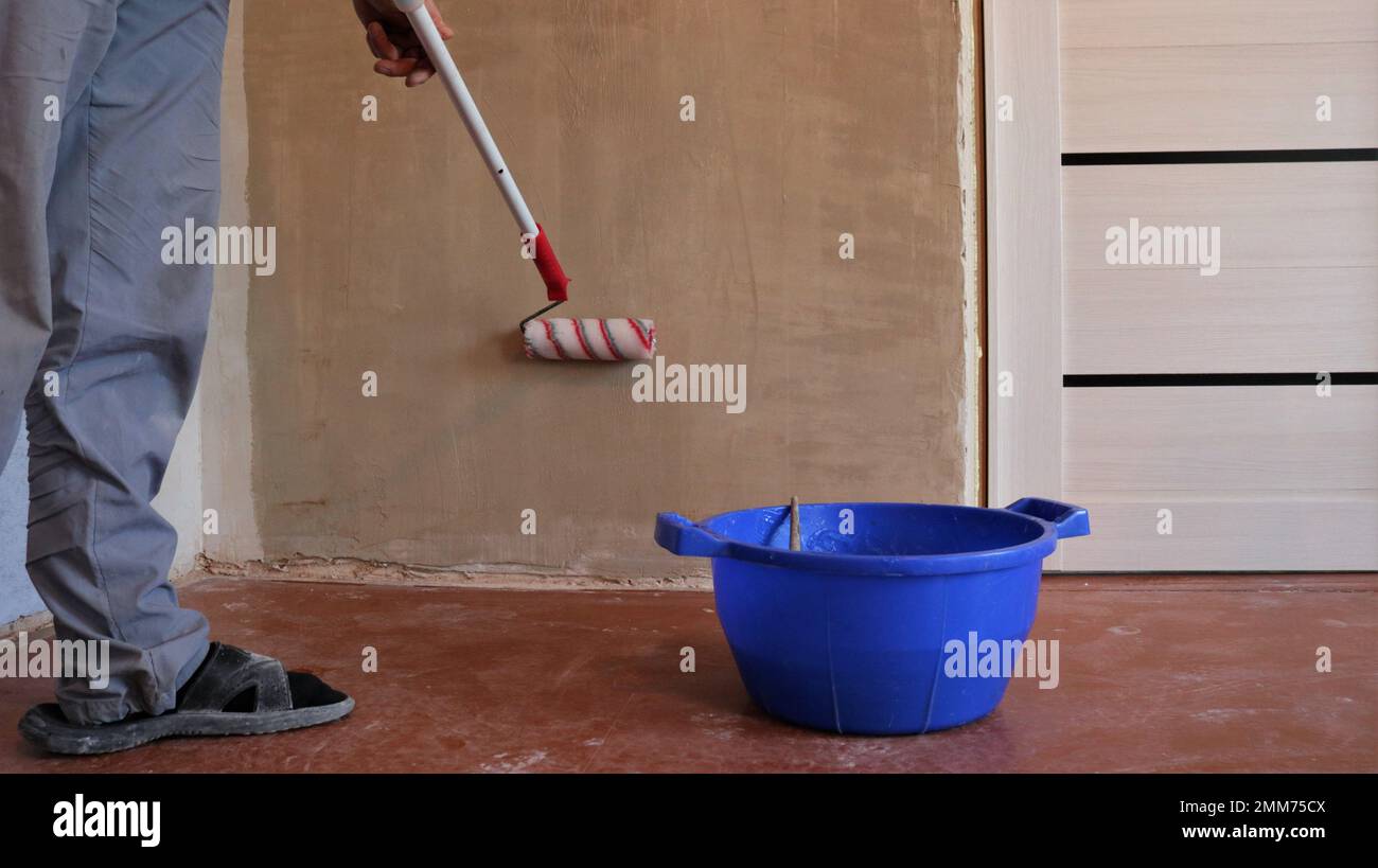 a man applies glue or a primer solution with a striped roller with a ...