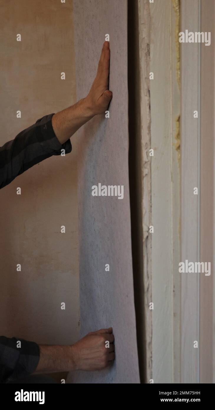 male hands pressing a strip of wallpaper against the wall side view ...