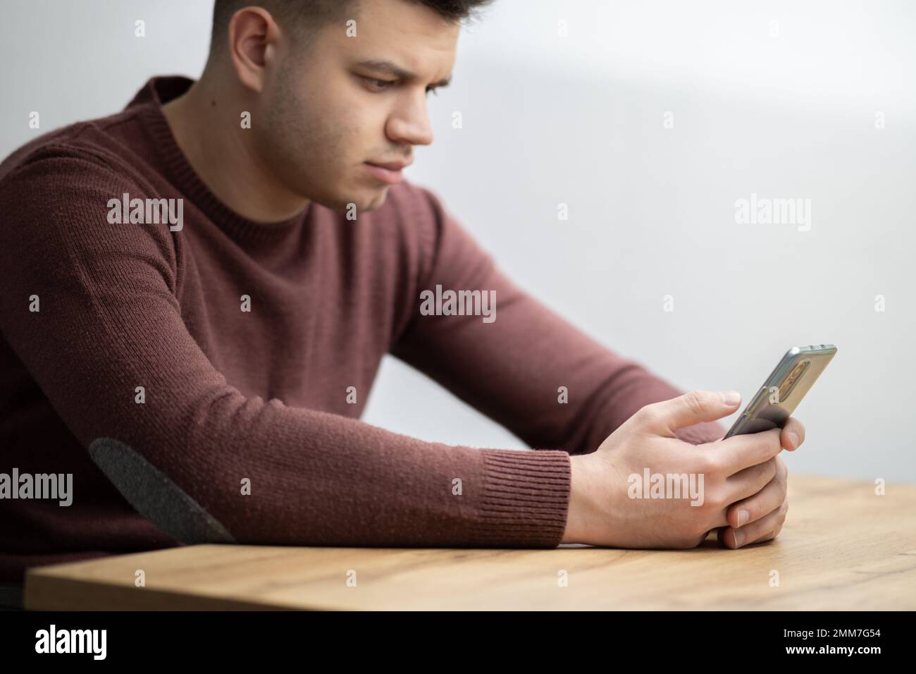 Man sitting on desk and using smartphone. Close up of a man in sweater ...