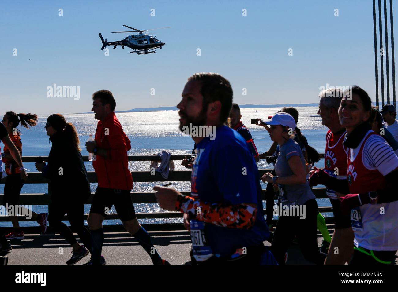 A NYPD helicopter flies in the background as runners cross the ...