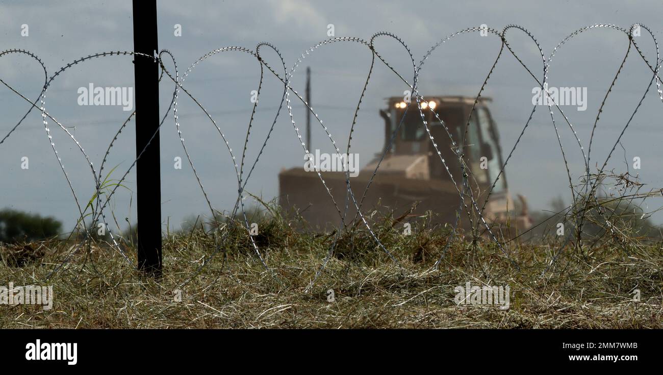 A tractor levels an area for tents to be erected behind a razor wire ...