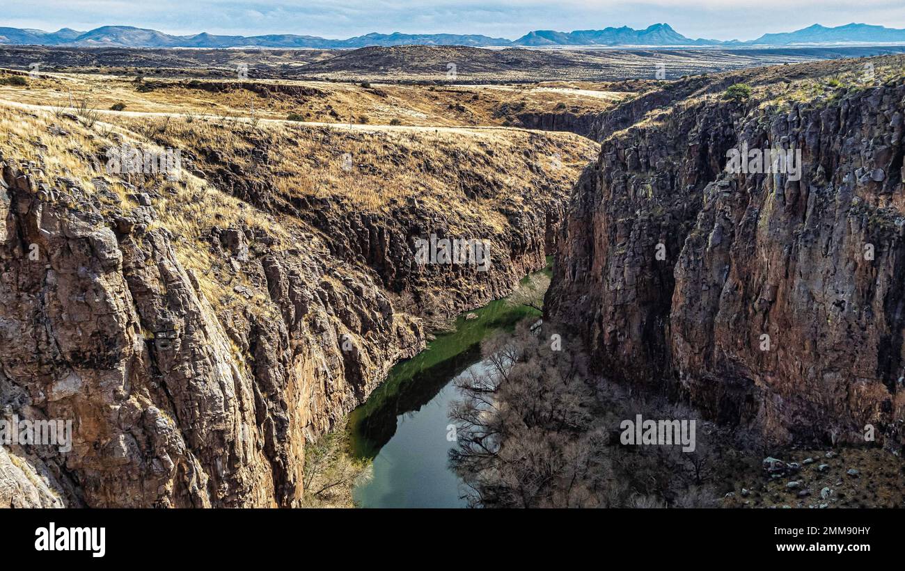 A desert cliff overlooks a tranquil stream winding through barren sands ...
