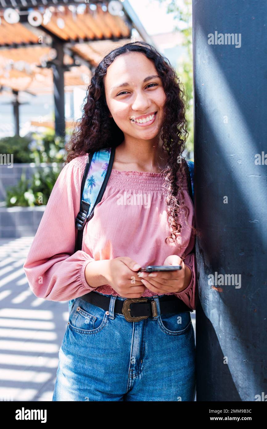 Latin university student woman smiling and using her mobile sitting ...