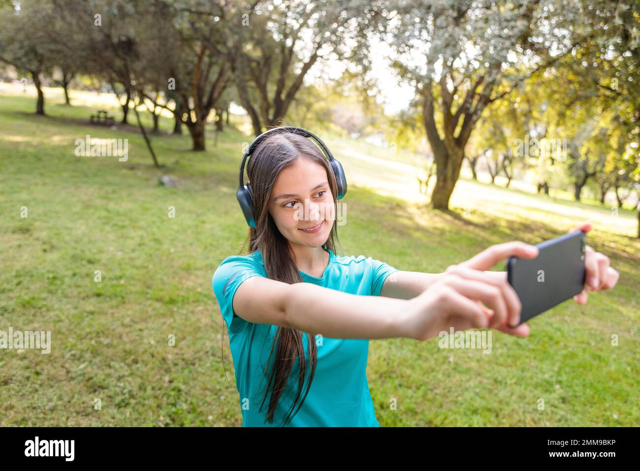 Smiling teenage girl wearing a turquoise t shirt and headphones, taking ...