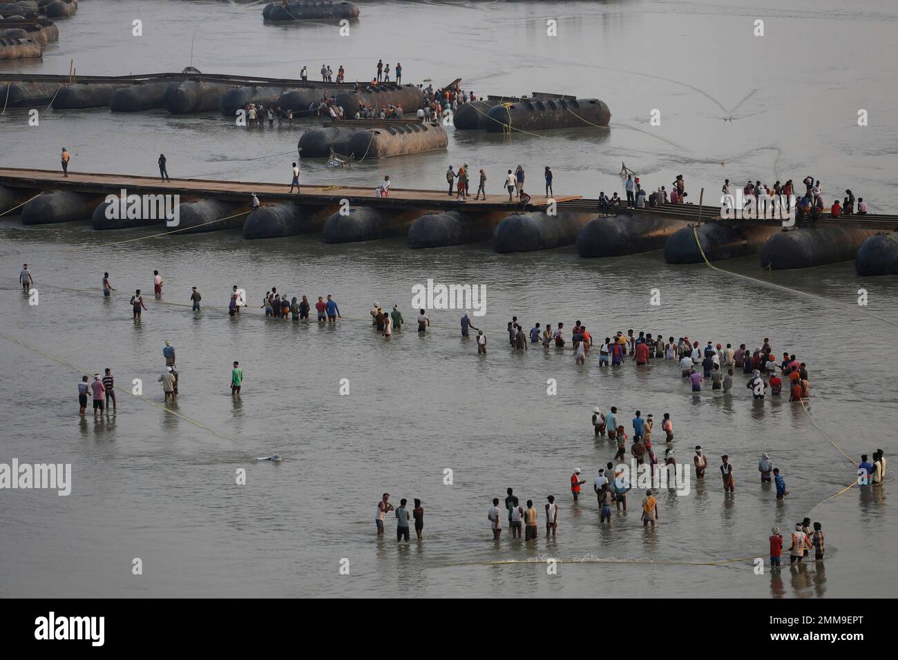 Indian laborers pull a pontoon buoy with a rope in the river Ganges as ...