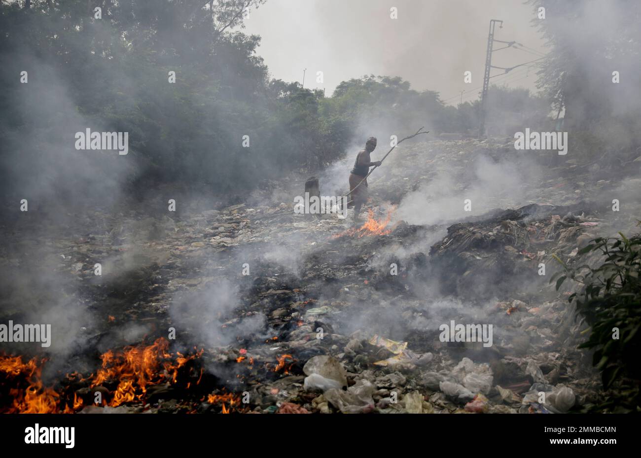 A heap of garbage is set on fire as an Indian man walks past in New ...