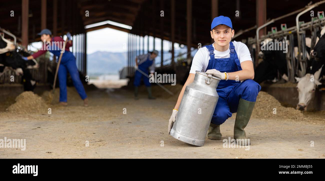 Male farm worker carrying big milk can walking in cowshed on dairy farm ...