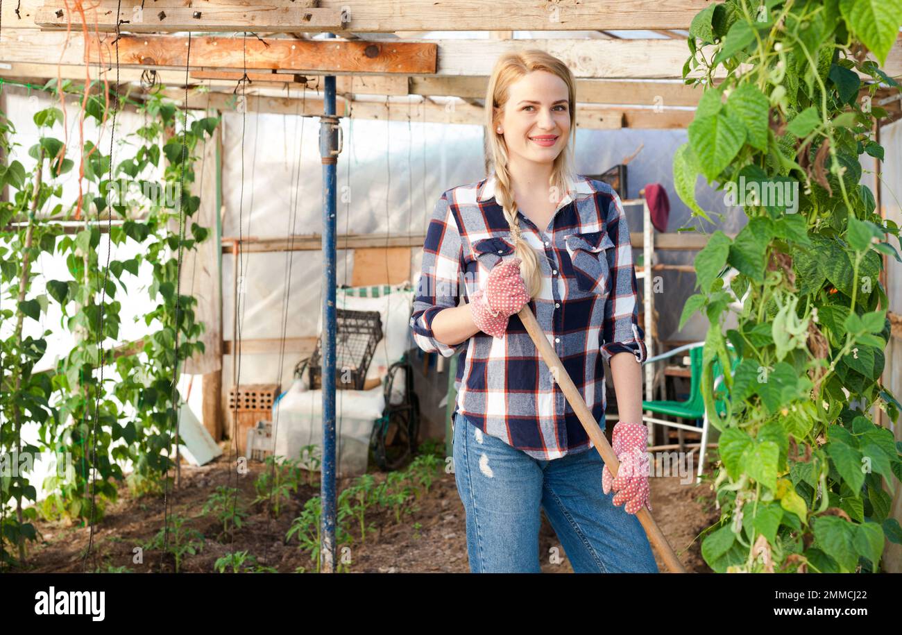 Young woman gardener using mattock at hothouse with green seedlings ...