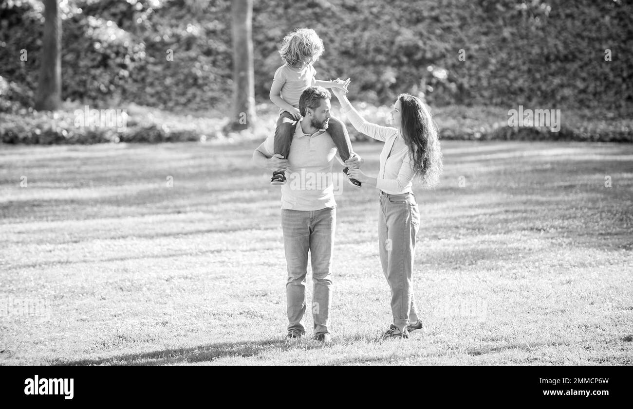 Happy mother and father carrying boy child on shoulders summer outdoors ...