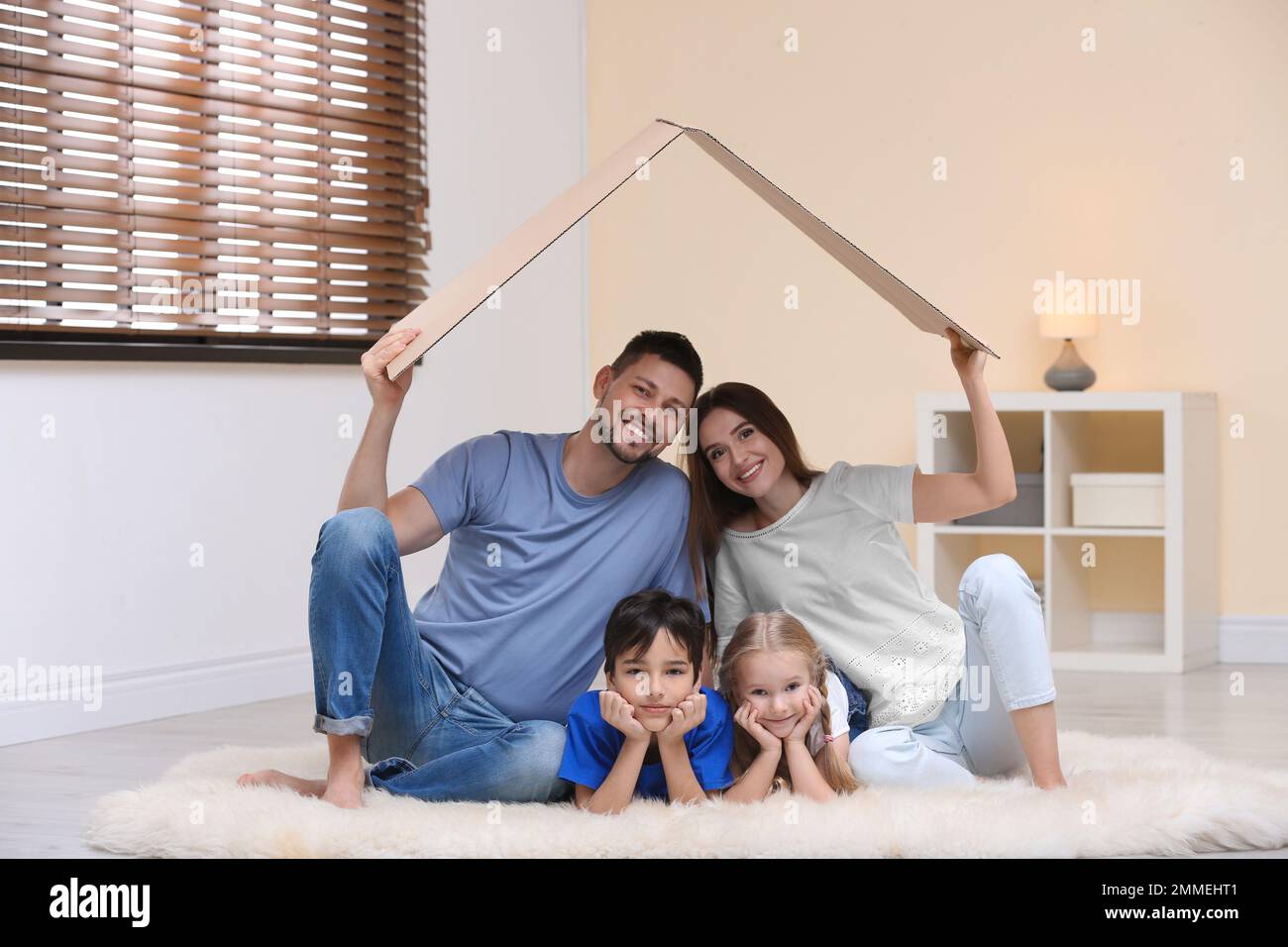 Happy family sitting under cardboard roof at home. Insurance concept ...