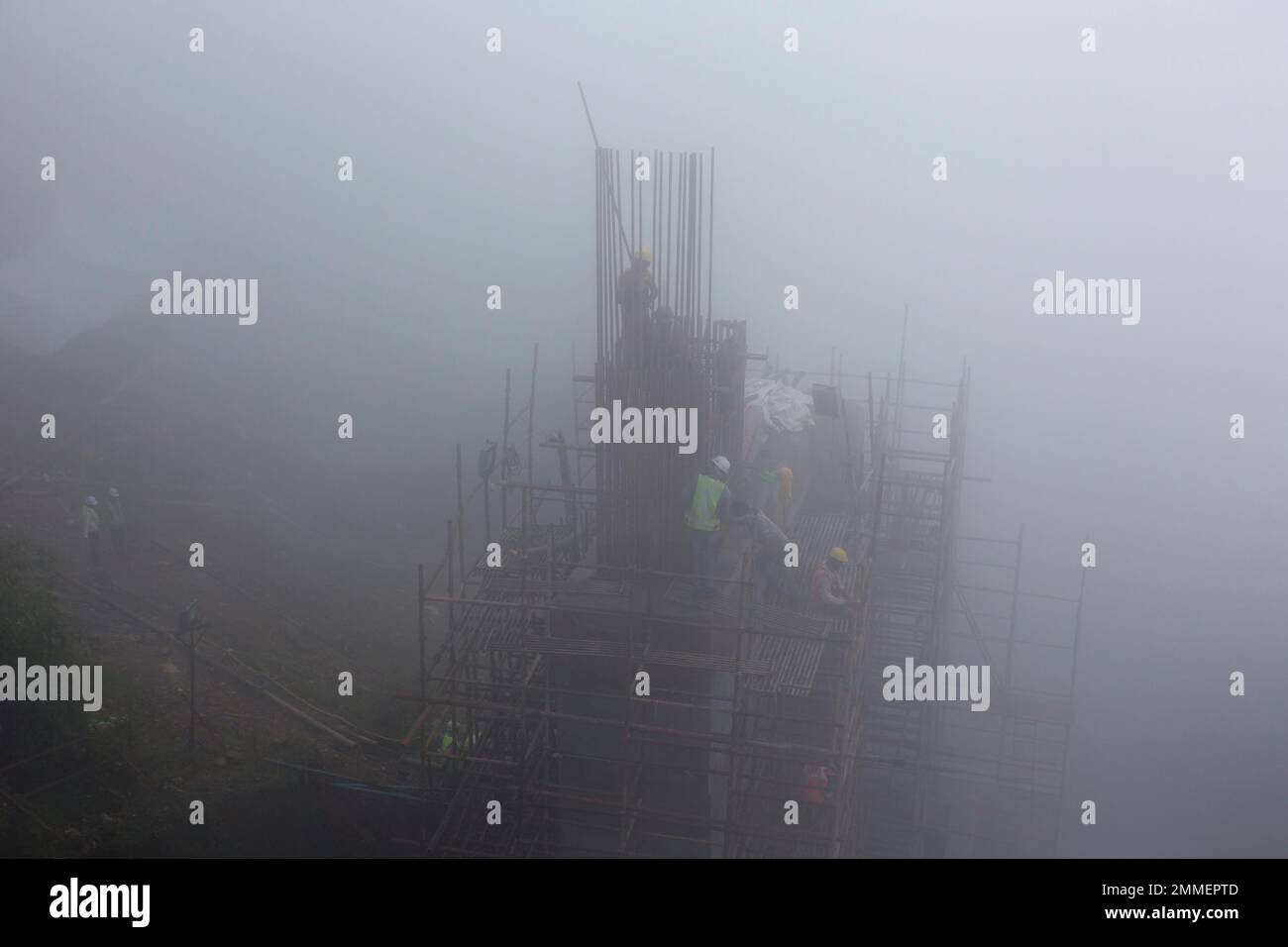 A construction crew works under a thick fog on a tower which is a part ...
