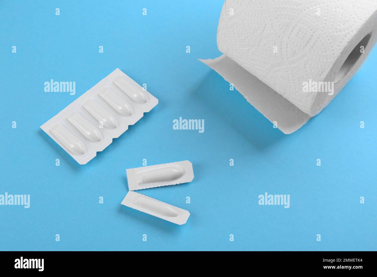 Suppositories and toilet paper on light blue background, flat lay ...