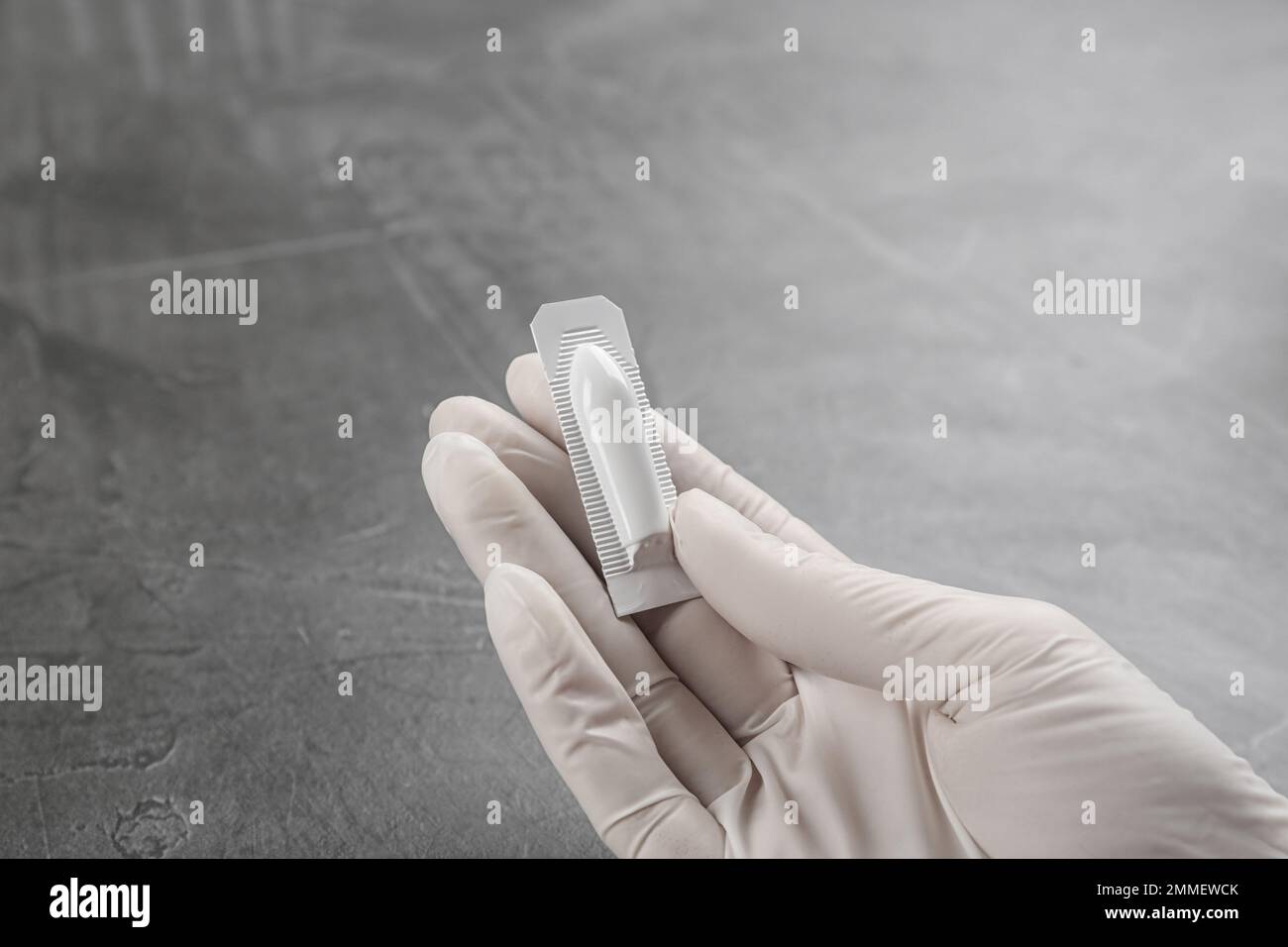 Woman holding suppository at grey table, closeup. Hemorrhoid treatment ...