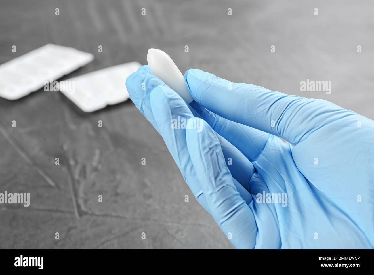Woman holding suppository at grey table, closeup. Hemorrhoid treatment ...