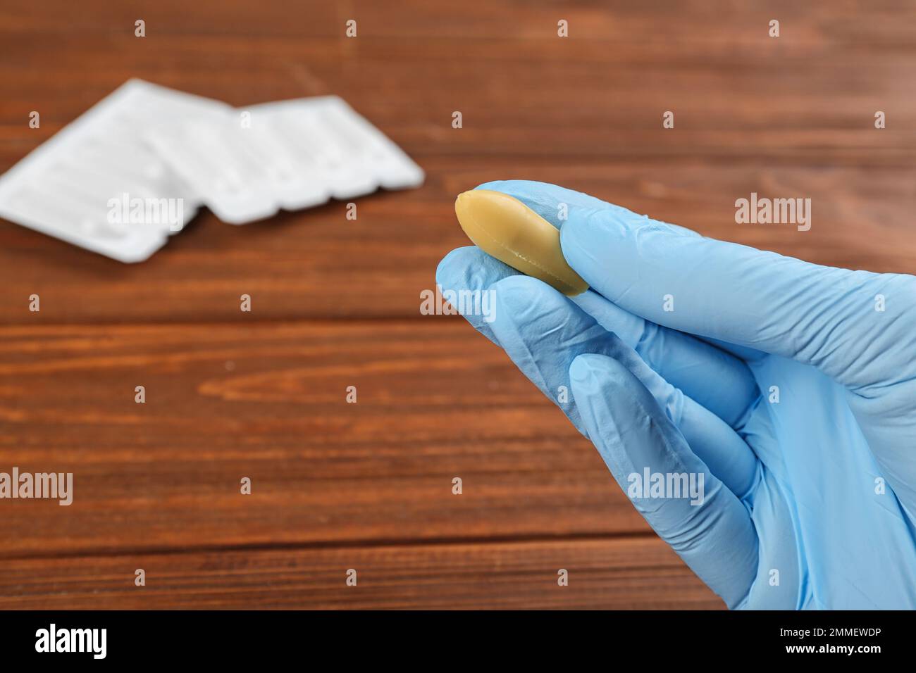 Woman holding suppository at wooden table, closeup. Hemorrhoid ...
