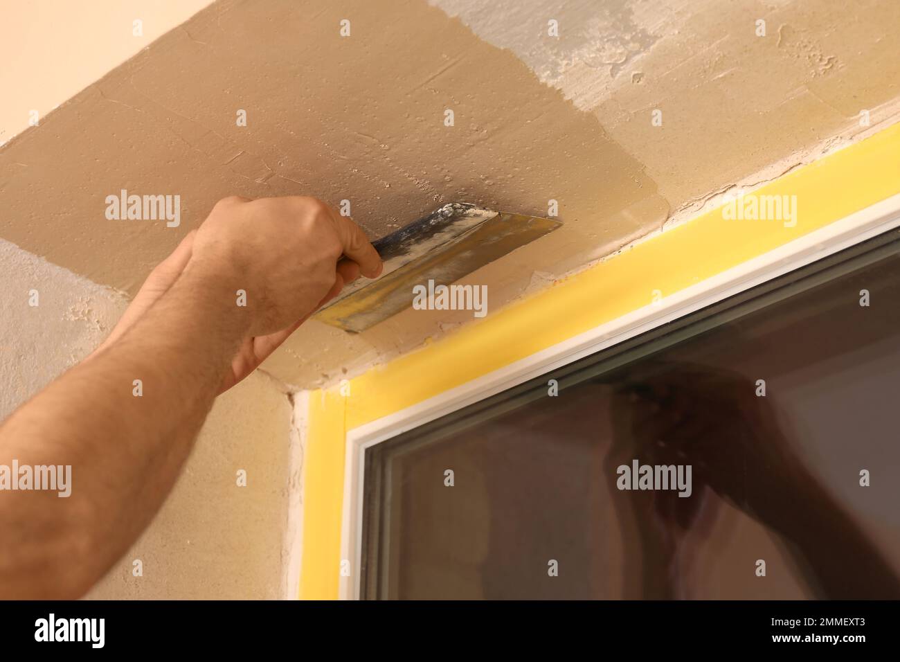 Man plastering window area with putty knife indoors, closeup. Interior ...