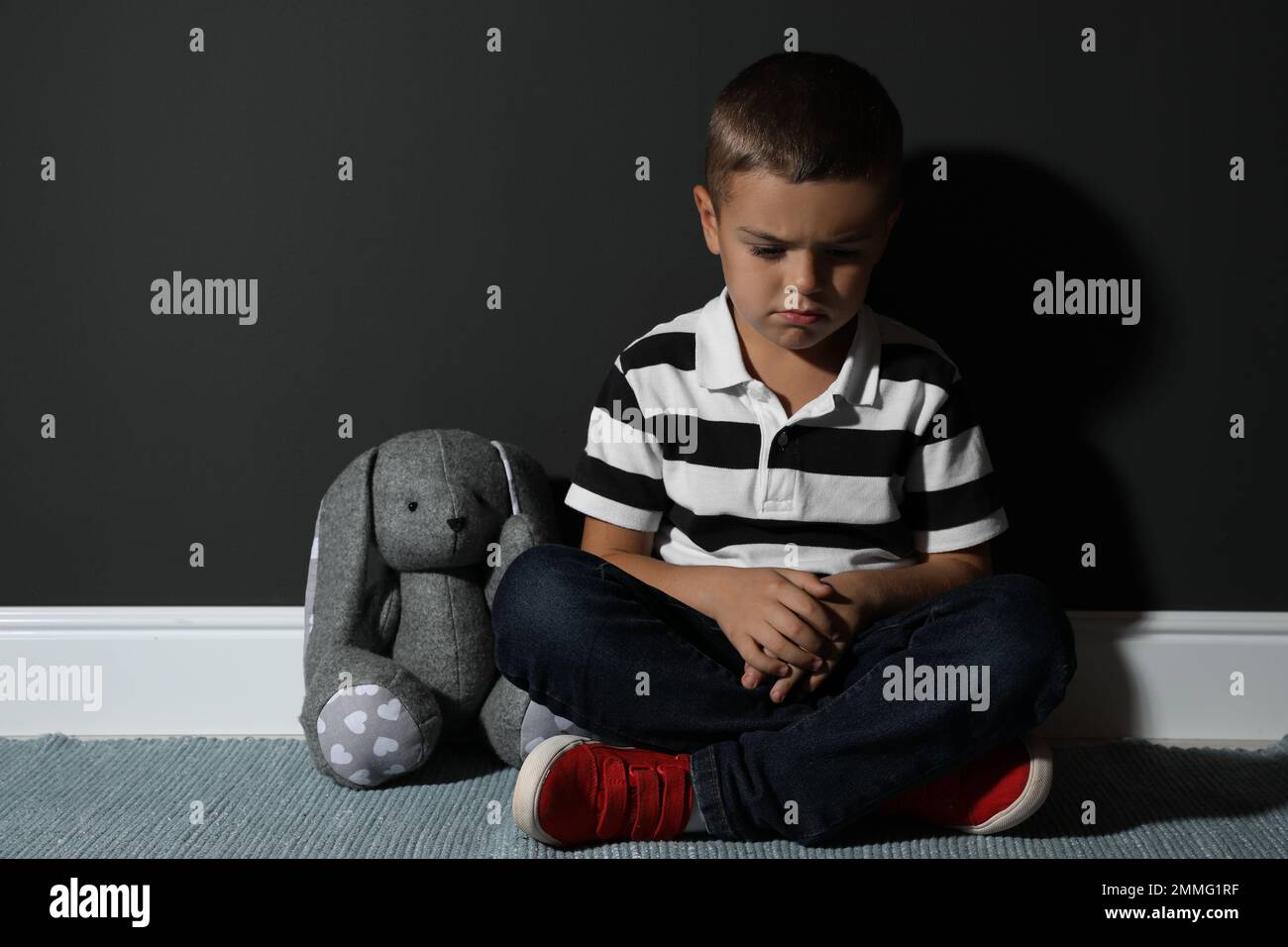Sad little boy with toy near black wall. Domestic violence concept ...