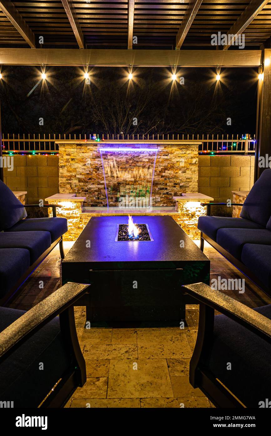 A resort style backyard at night with a waterfall, pergola, and a ...